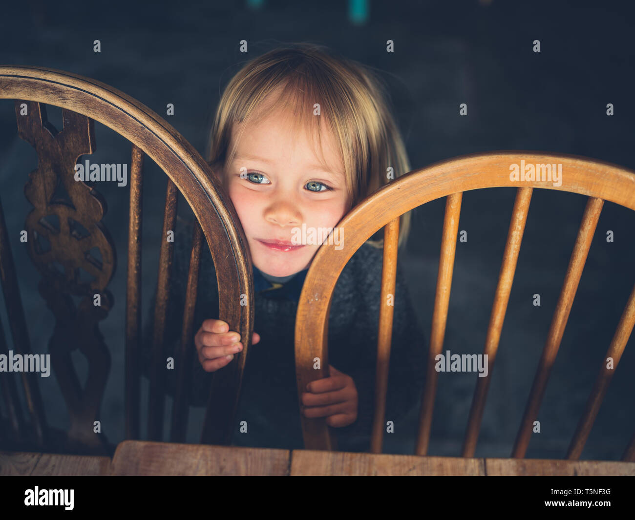 A little toddler is hiding behind some chairs in a cafe Stock Photo - Alamy