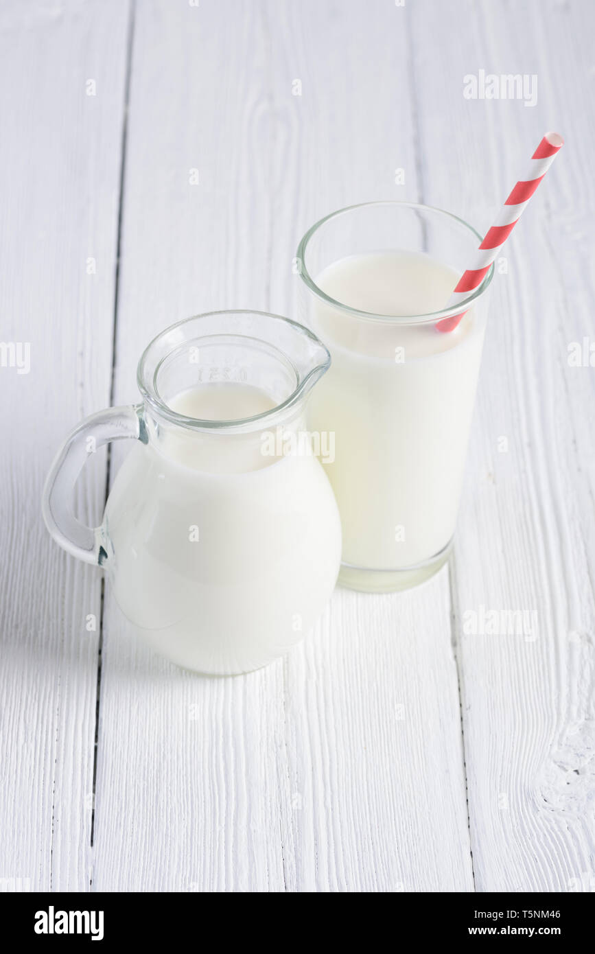 Glass of milk with stripped red paper straw and jug of milk on white ...