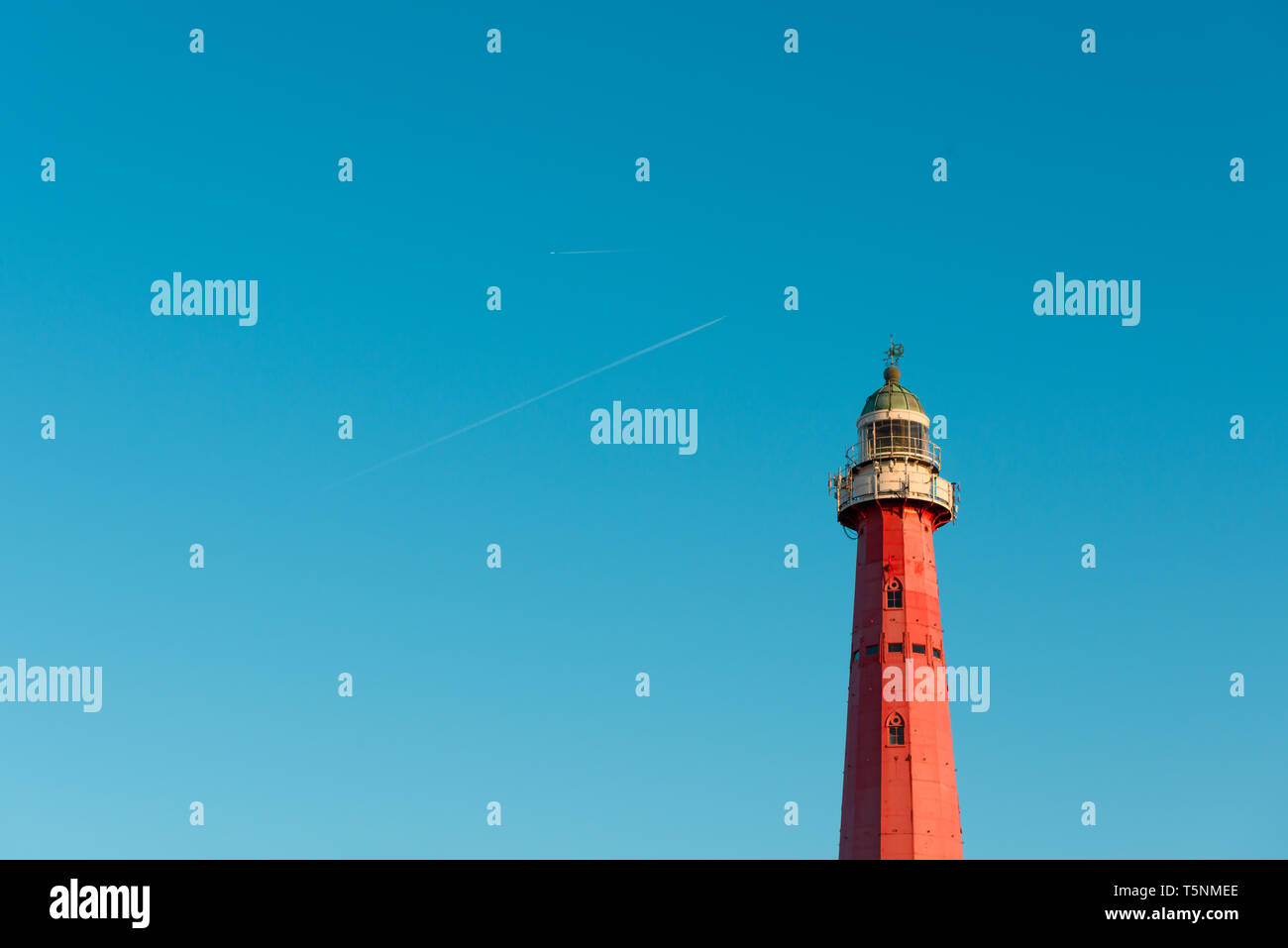 Vintage red iron lighthouse over blue sky background with airplane ...