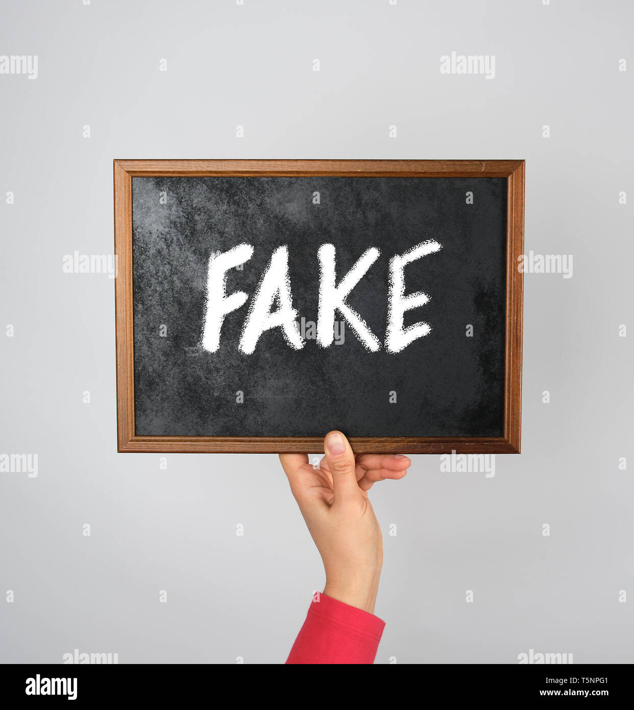 hand holding a black chalk board with the inscription fake, gray ...