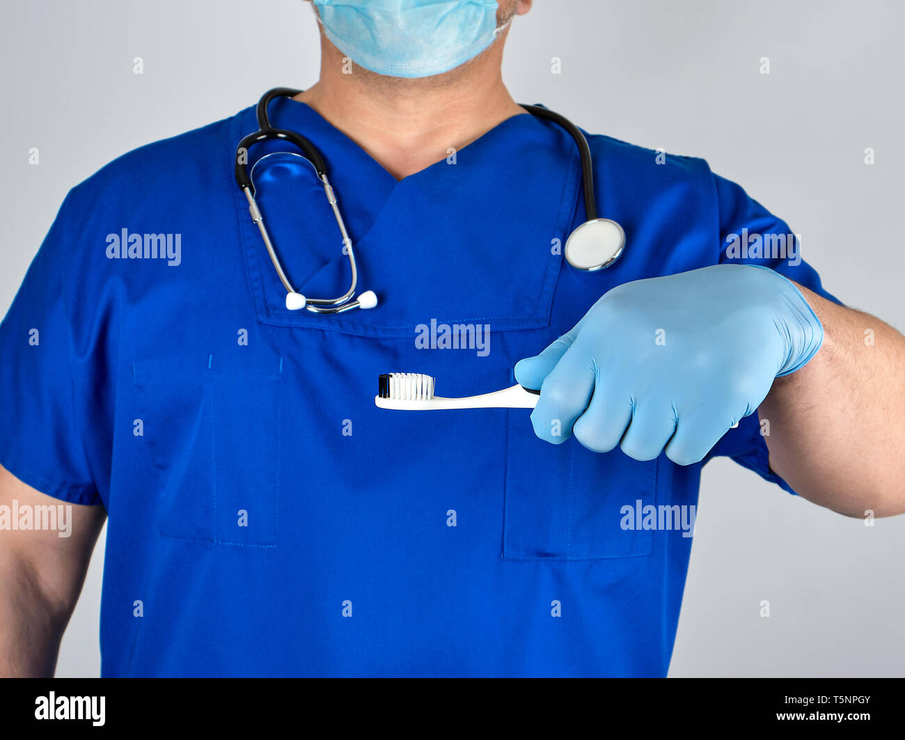 Doctor in sterile latex gloves and blue uniform holding a toothbrush ...