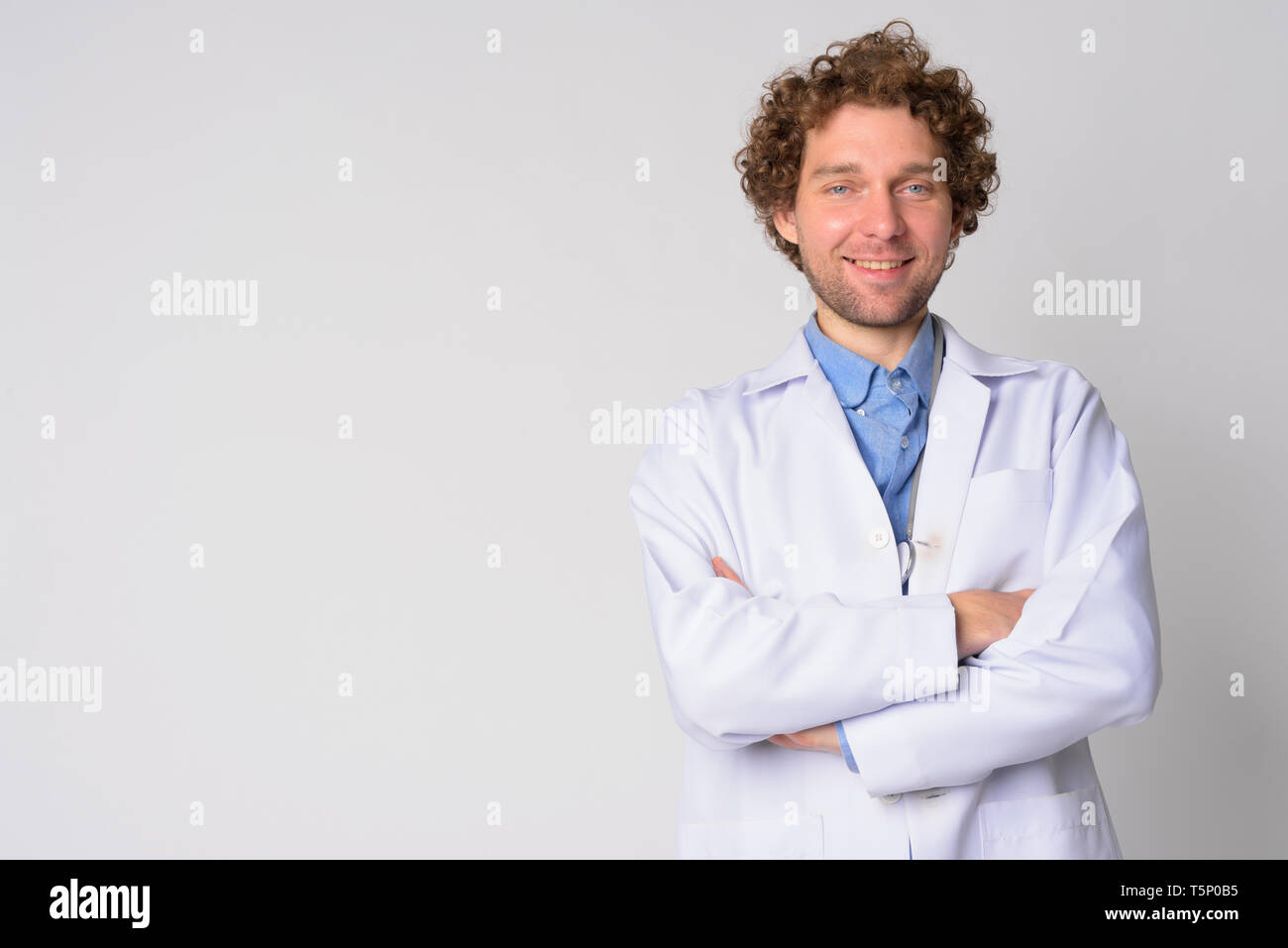 Happy handsome man doctor with curly hair smiling and crossing arms ...