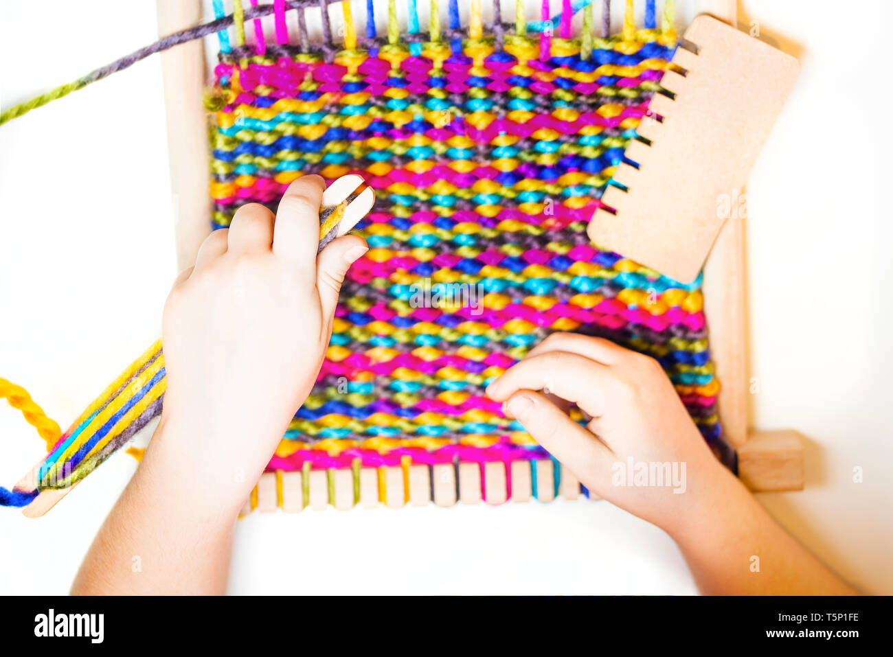Weaving. Hands of little caucasian girl holdig a shuttle. Working on ...