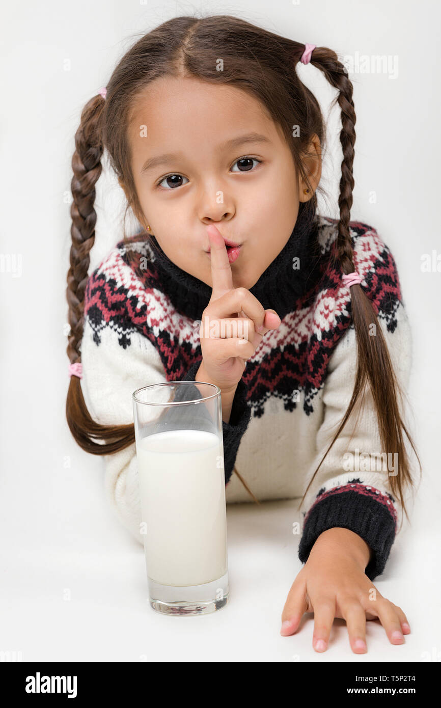 Portrait of cute little child girl holding glass of milk and showing ...