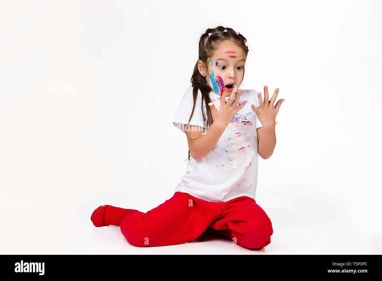 scared little child girl looks at his hands painted in colorful paint ...