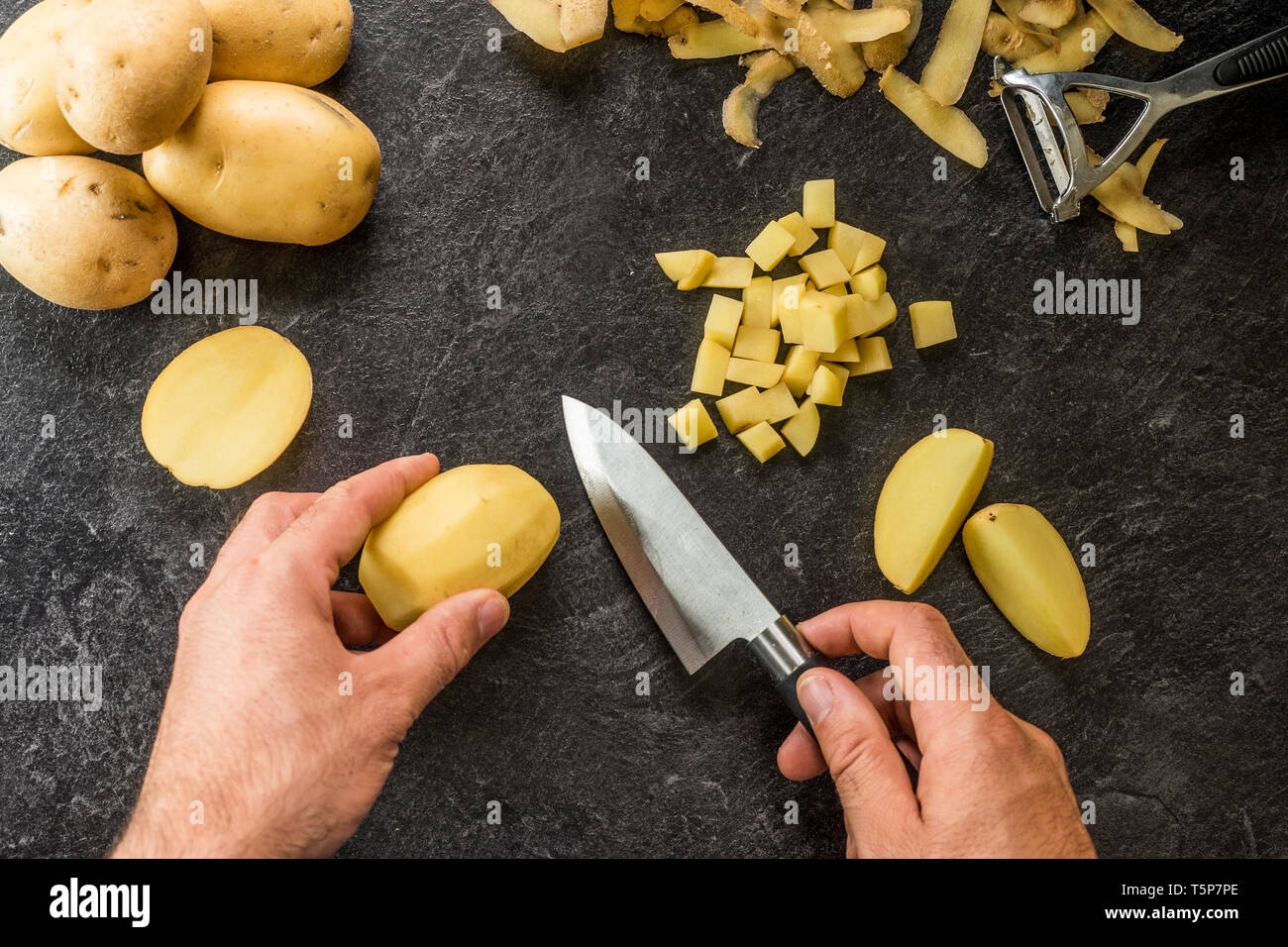 Hand cutting potatoes on textured black background. Photo from above ...
