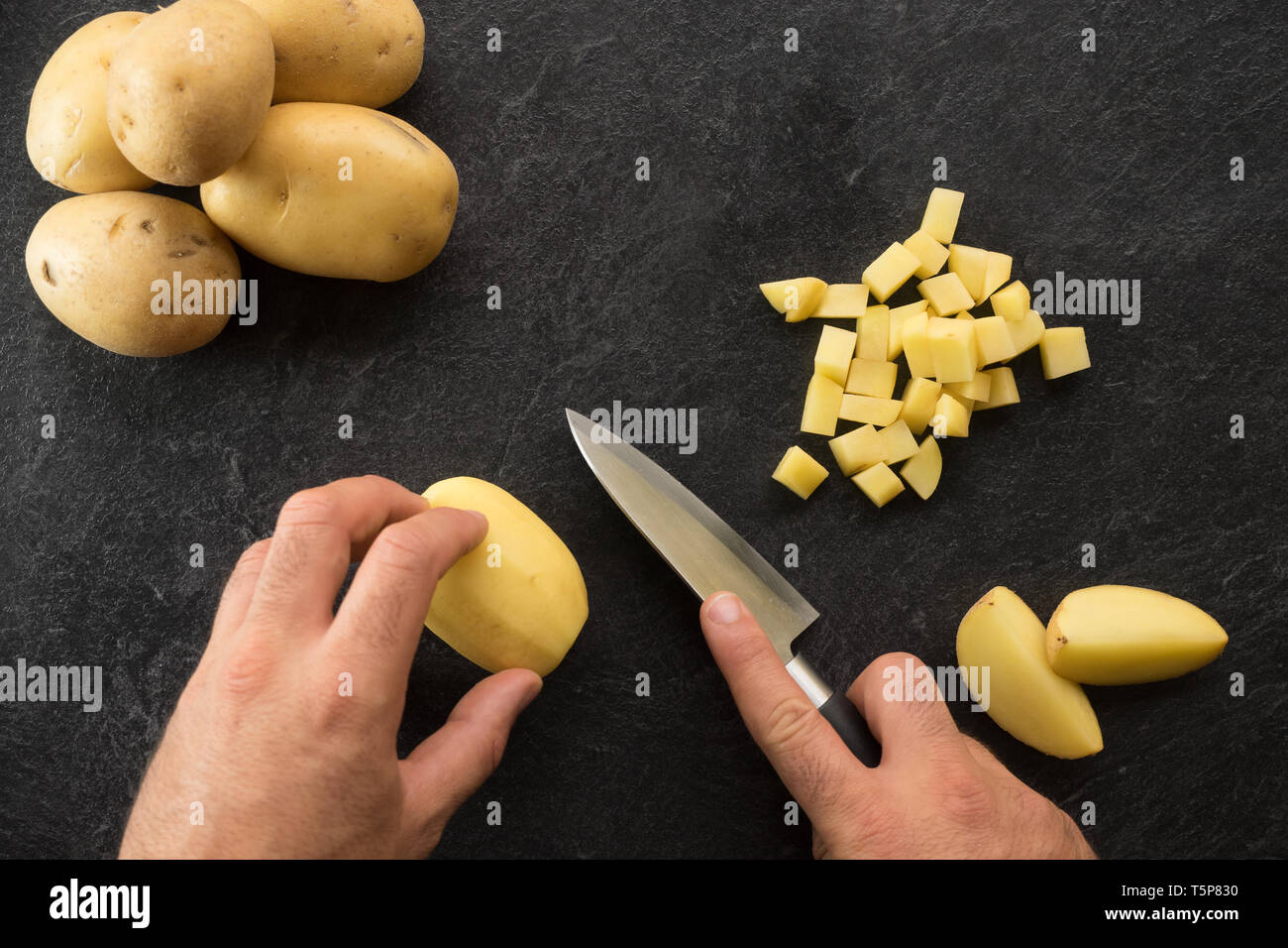 Hand cutting potatoes on textured black background. Photo from above ...