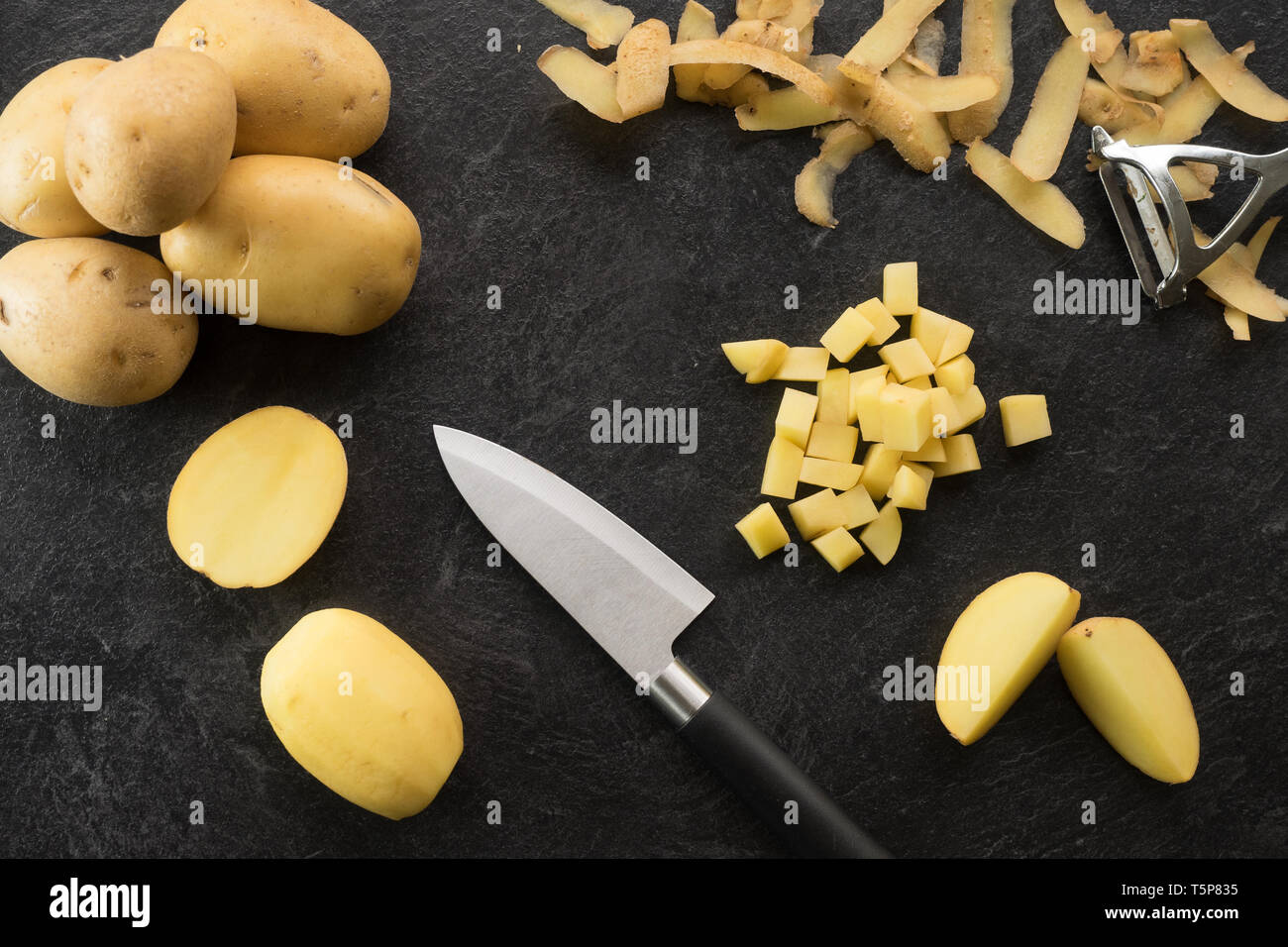 Knife cutting potatoes on textured black background. Photo from above ...