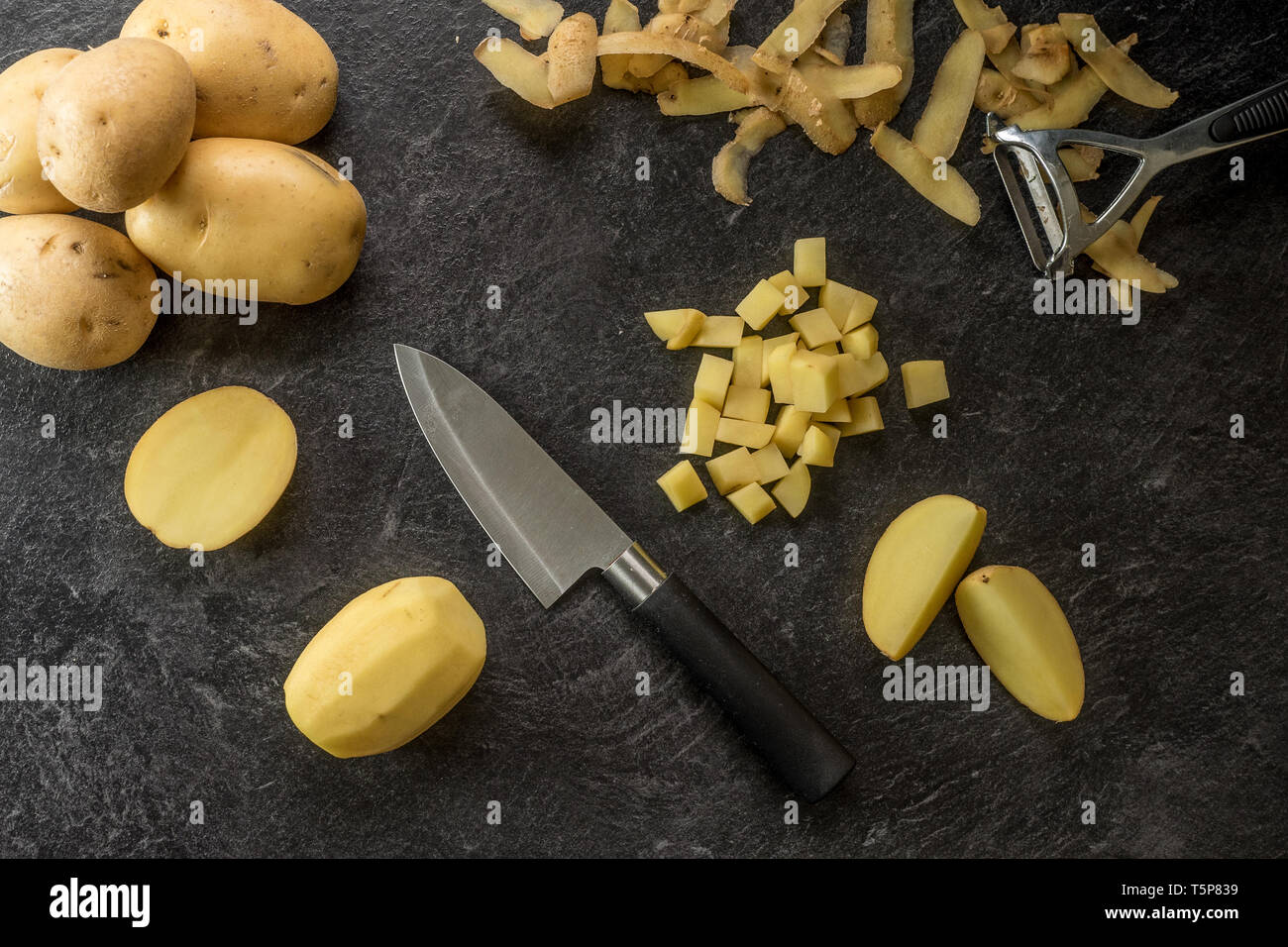 Knife cutting potatoes on textured black background. Photo from above ...