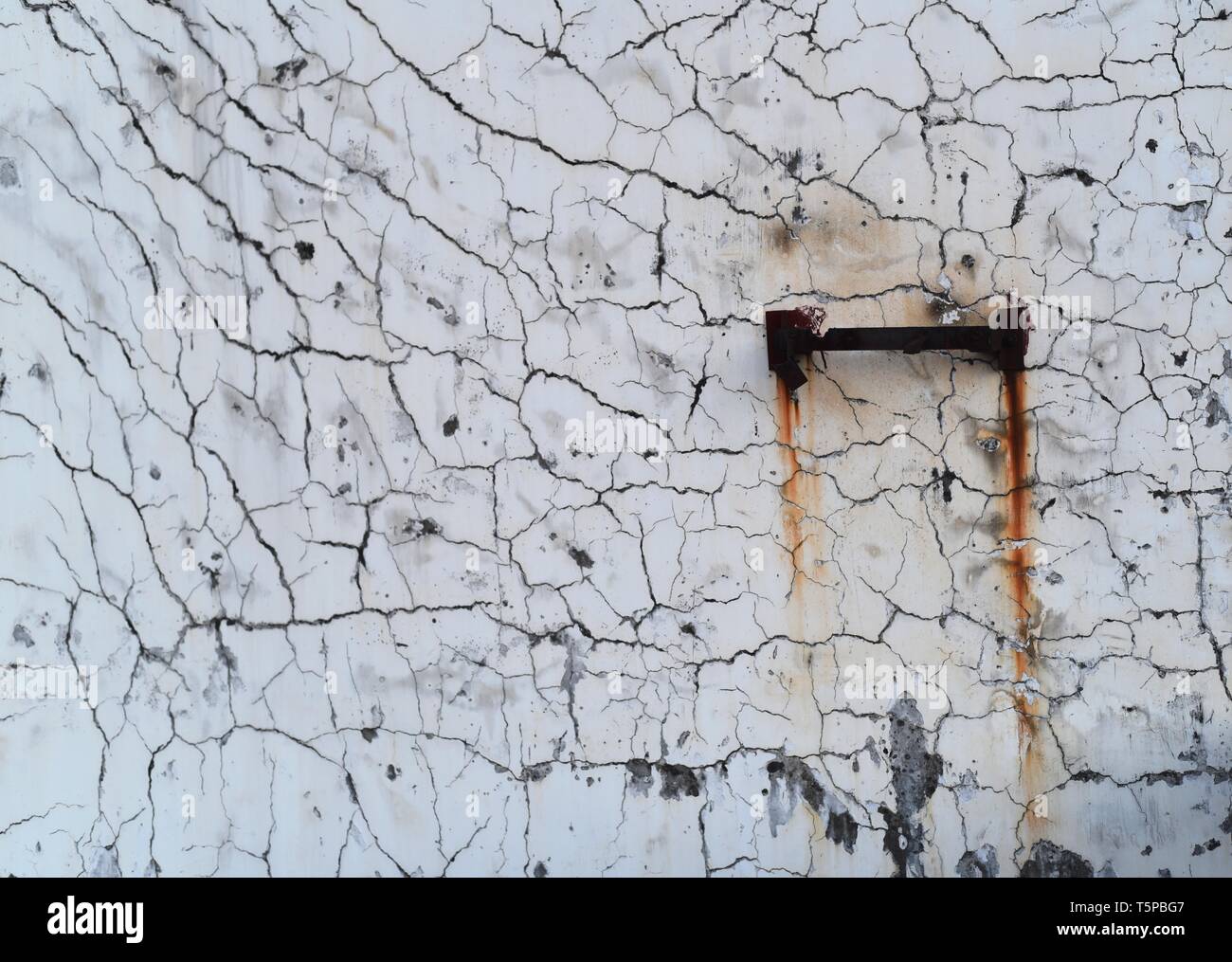 A mottled wall with numerous cracks and a rusty metallic bracket on the ...