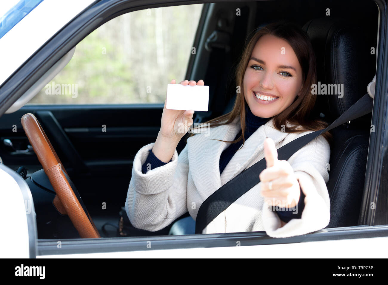 Beautiful young girl sitting in white car showing an empty white card ...
