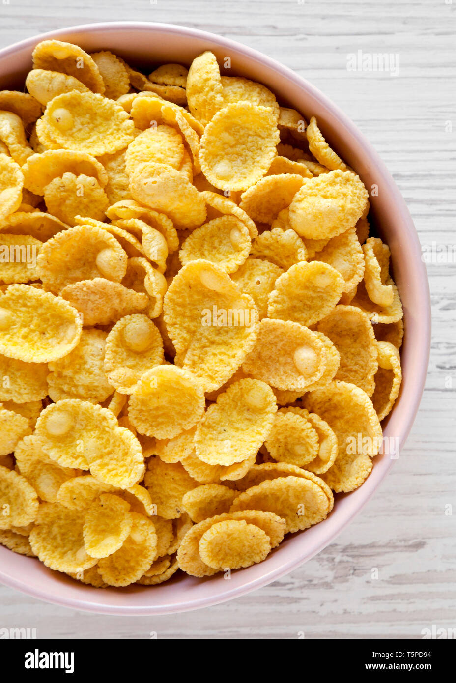 Crispy corn flakes in a pink bowl for breakfast over white wooden ...