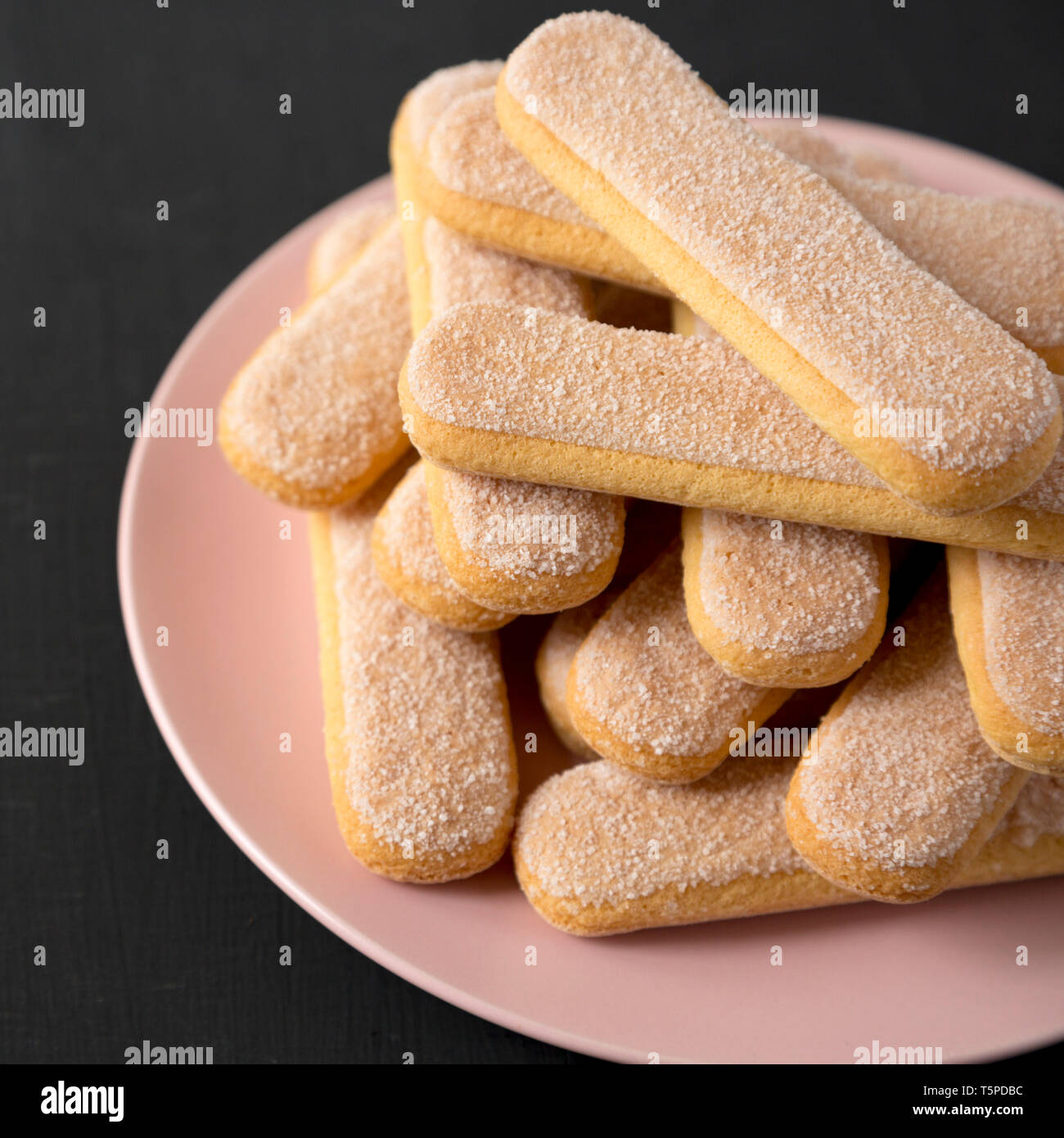 Savoiardi or ladyfingers cookies on a pink plate over black background ...