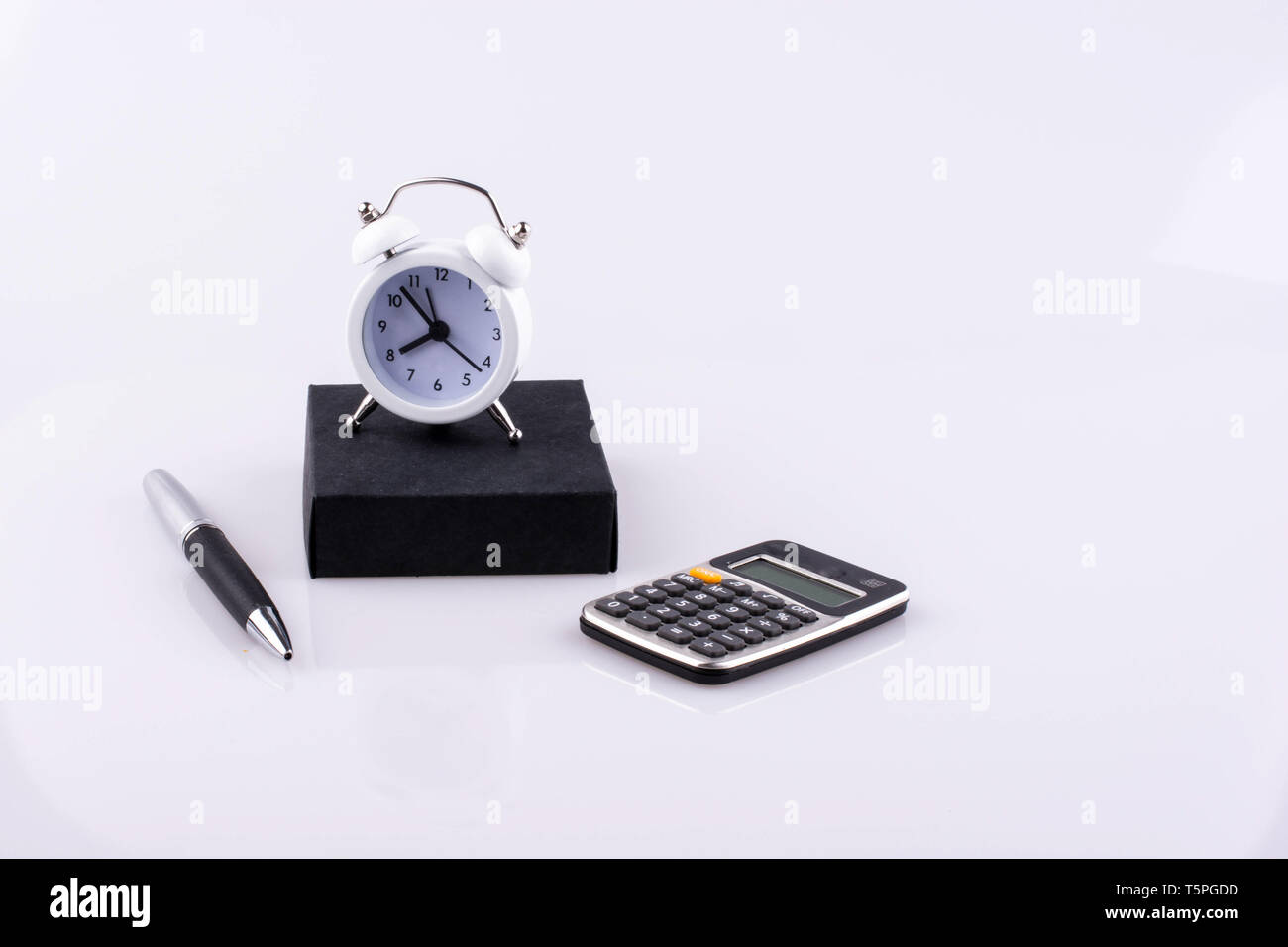 alarm clock, calculator, pen and a notebook placed on a white ...