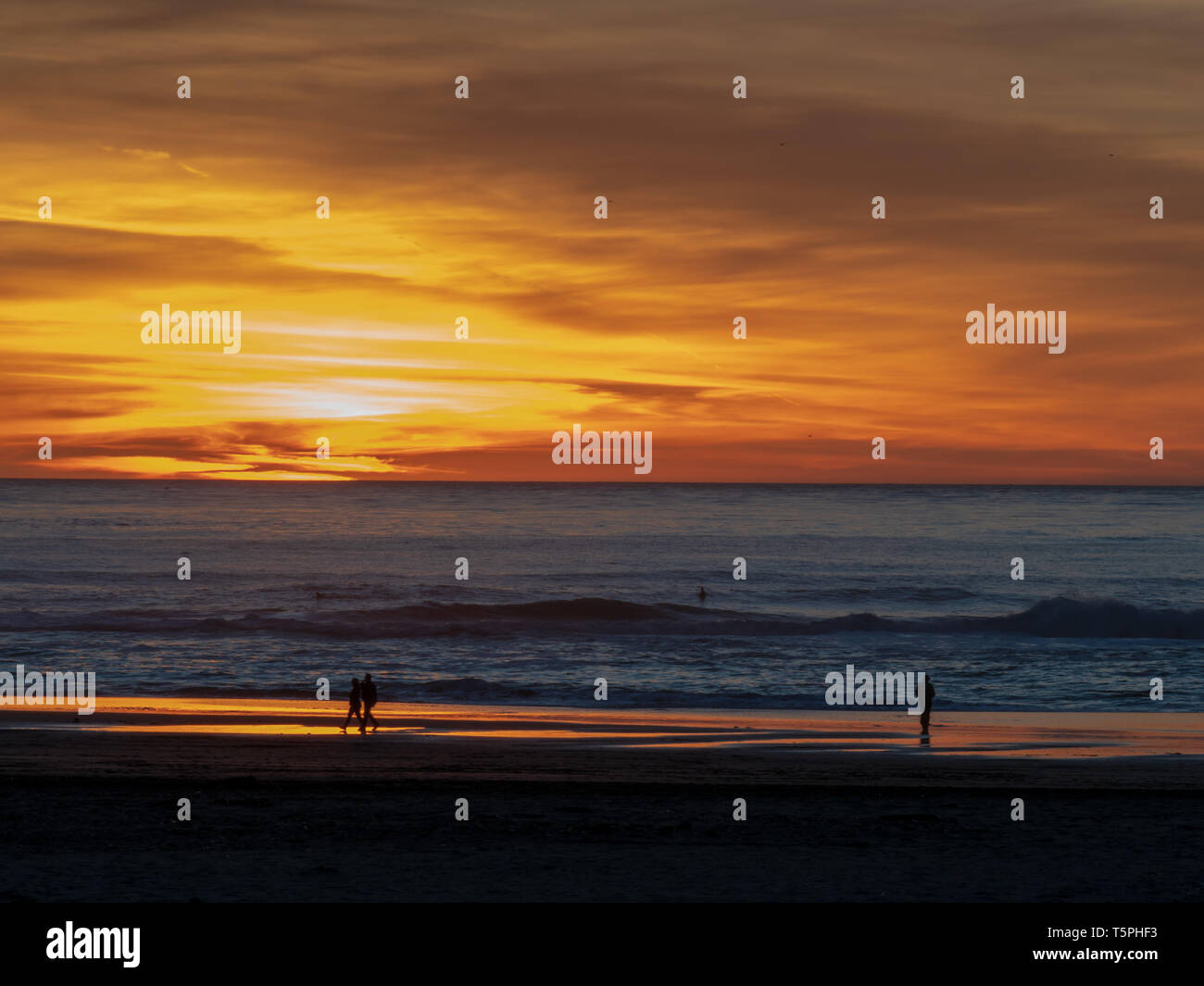 Sunset during dusk over Pacific Ocean with couples, surfers, and ...