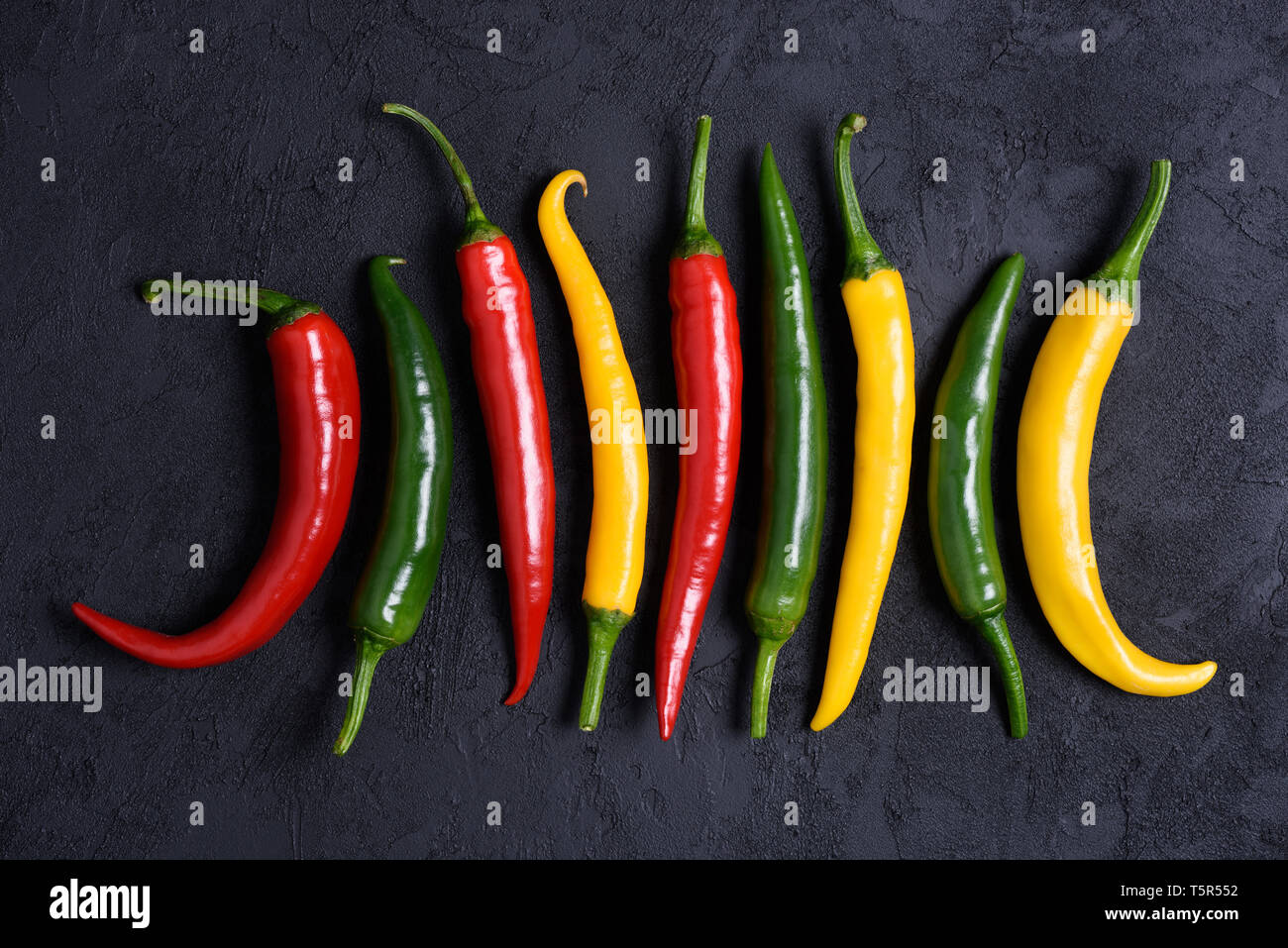 Different colored chili pepper on dark stone background Stock Photo - Alamy