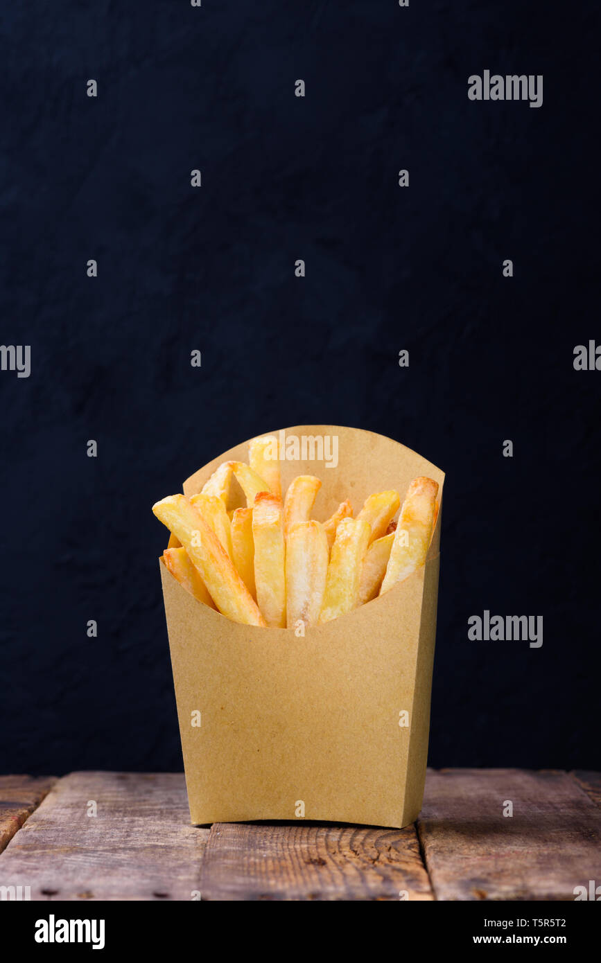 French fries in brown paper basket on wooden table with dark background ...