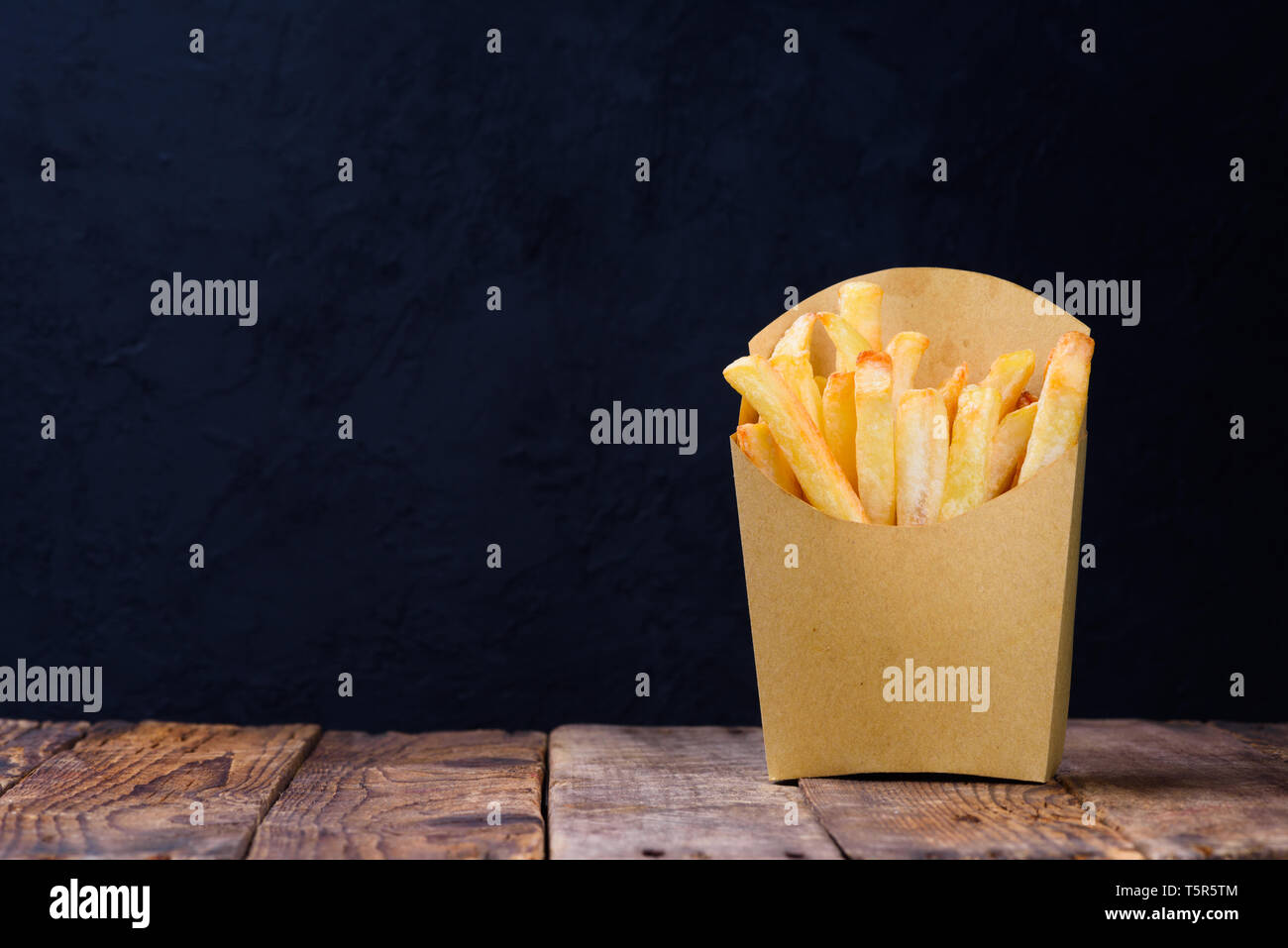 French fries in brown paper basket on wooden table with dark background ...