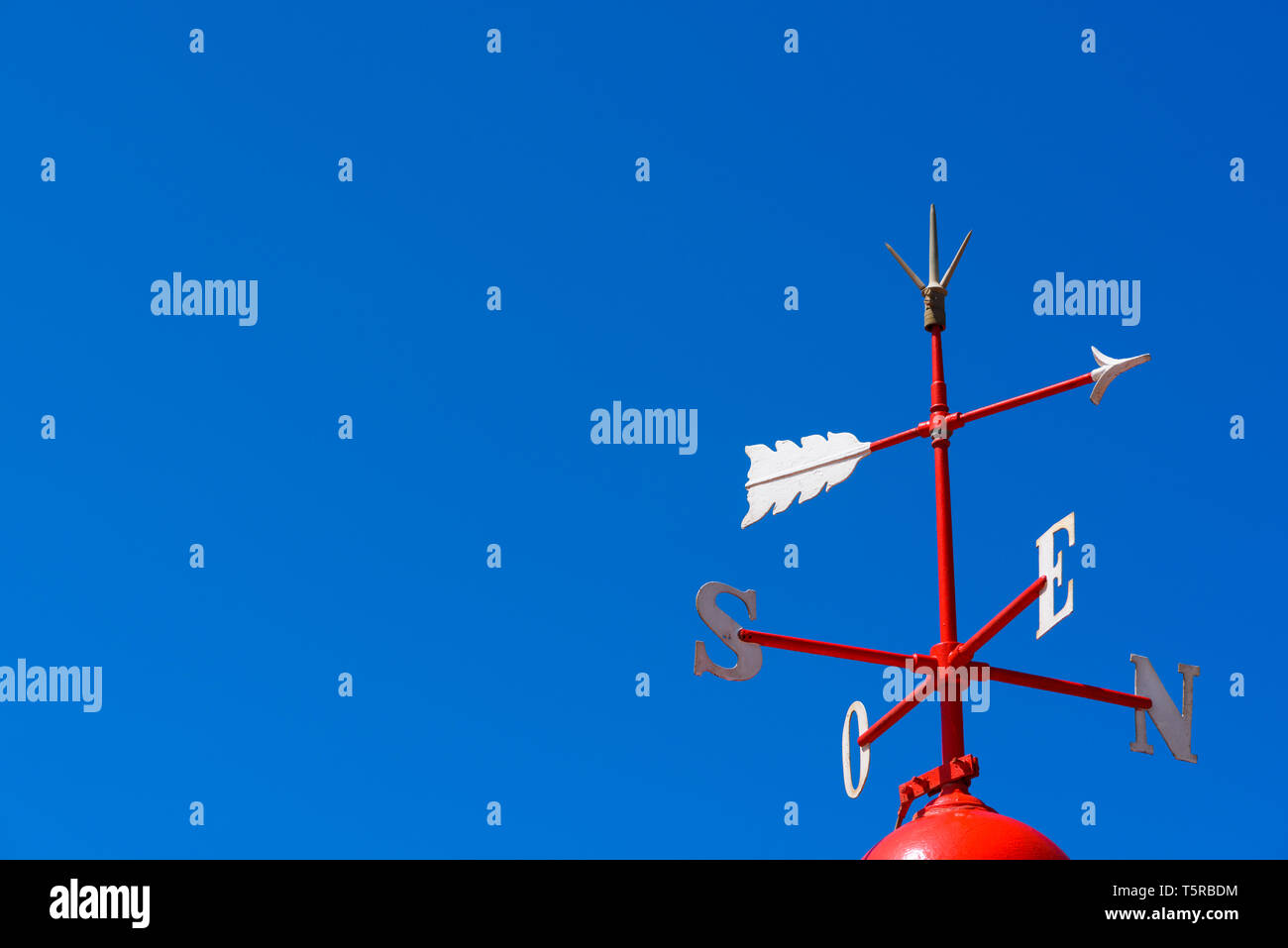 Red and white painted metal wind vane with arrow over blue summer sky ...