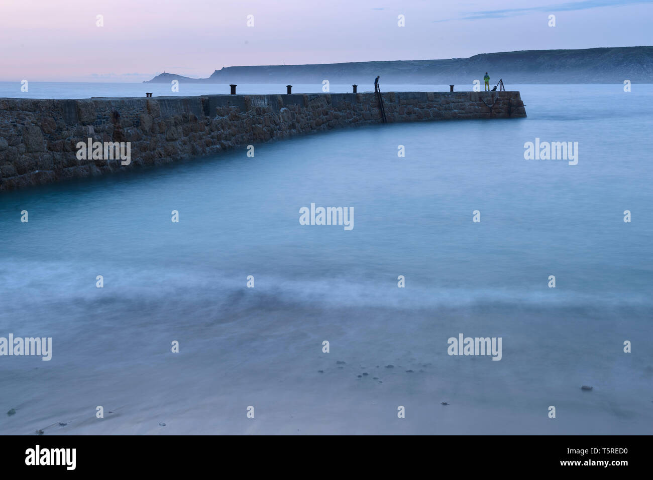 The harbour wall and beach at Sennen Cove, Cornwall, at sunset on a ...
