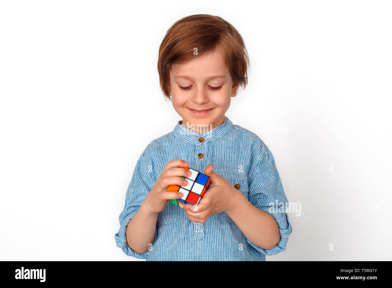 Little boy studio standing isolated on grey wall solving rubik's cube ...