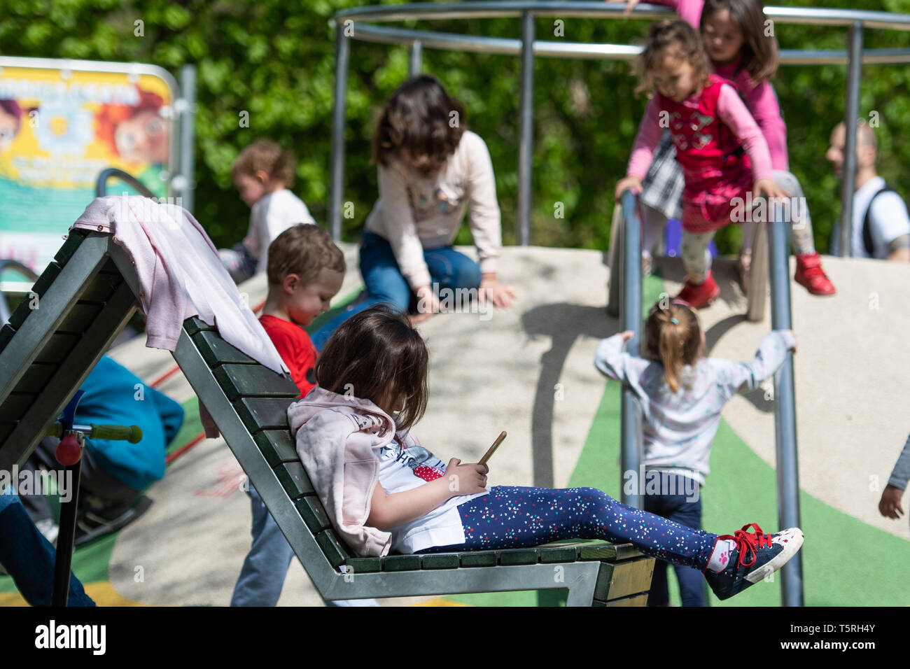 A small girl watches her phone as other children play in on the ...