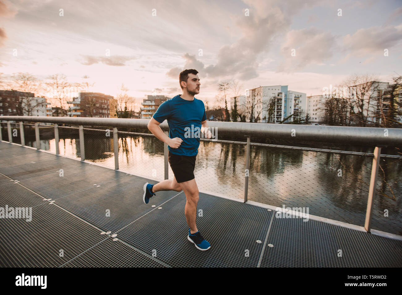 Young athletic man practicing sport outdoors, running fast along bridge ...