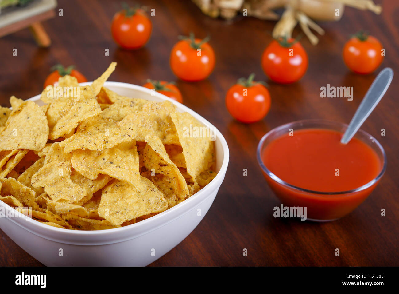 Yellow nacho in white bowl on the wooden table with tomato and ketchup ...