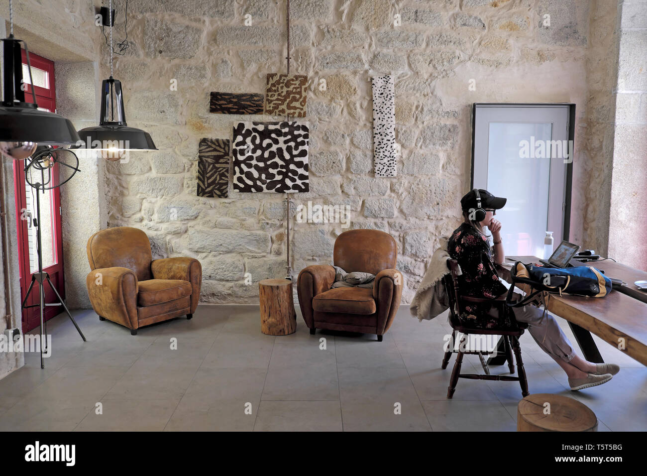 Trendy young woman plugged into laptop in computer lounge with art on ...