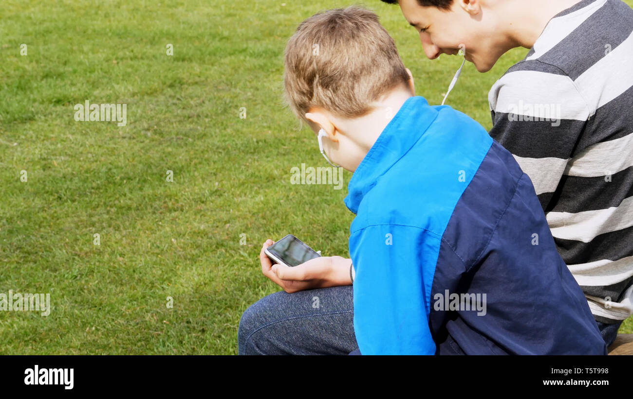 teen boys with smart phone listening or talking in british park on ...