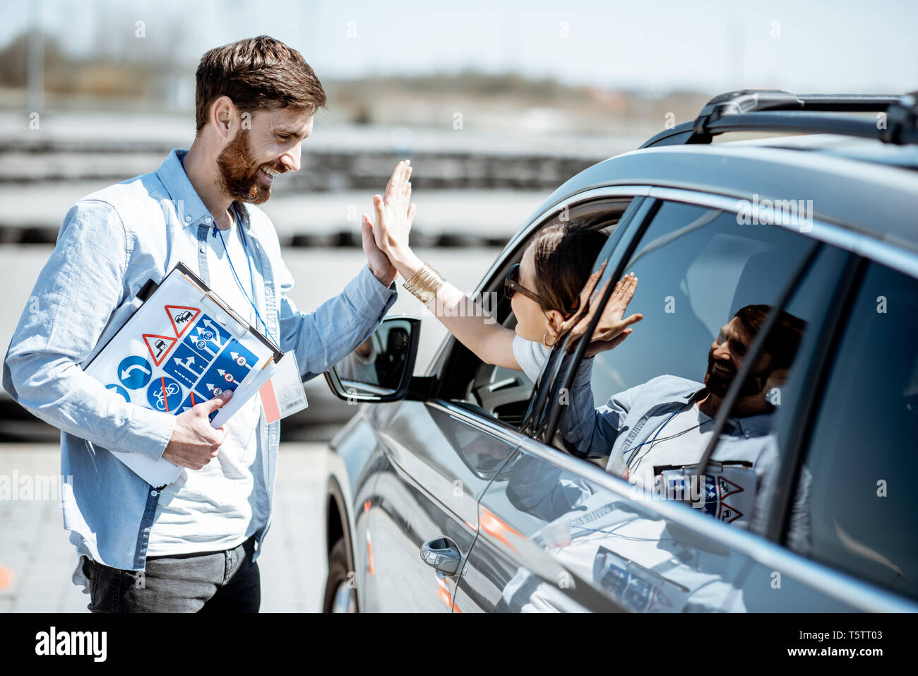 Instructor giving a five to a woman driver sitting in the car while ...