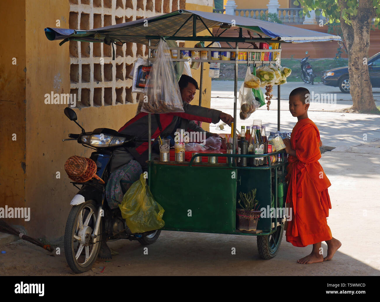Outside the walls of Wat Kampong Thom a child monk buys a meal form a ...