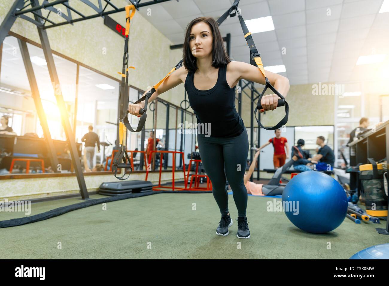 Young beautiful sporty woman exercising on fitness straps system in gym ...