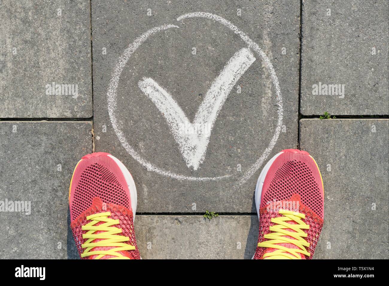 Checkmark ok sign on gray sidewalk with woman legs in sneakers, top ...