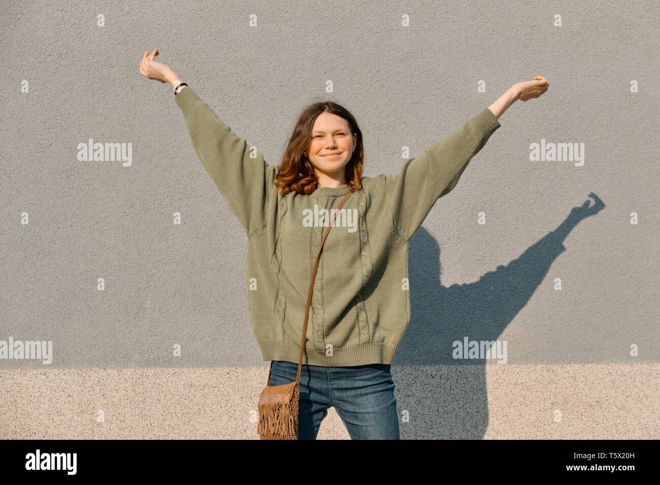 Outdoor portrait of smiling teen girl with arms raised up, gray sunny ...