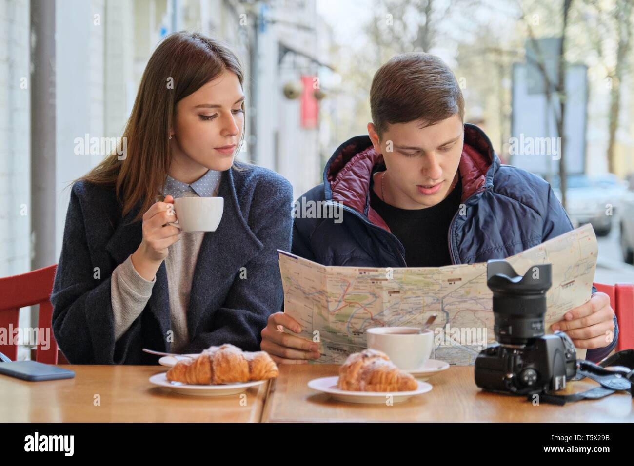 Young tourists man and woman reading map of city in outdoor cafe ...