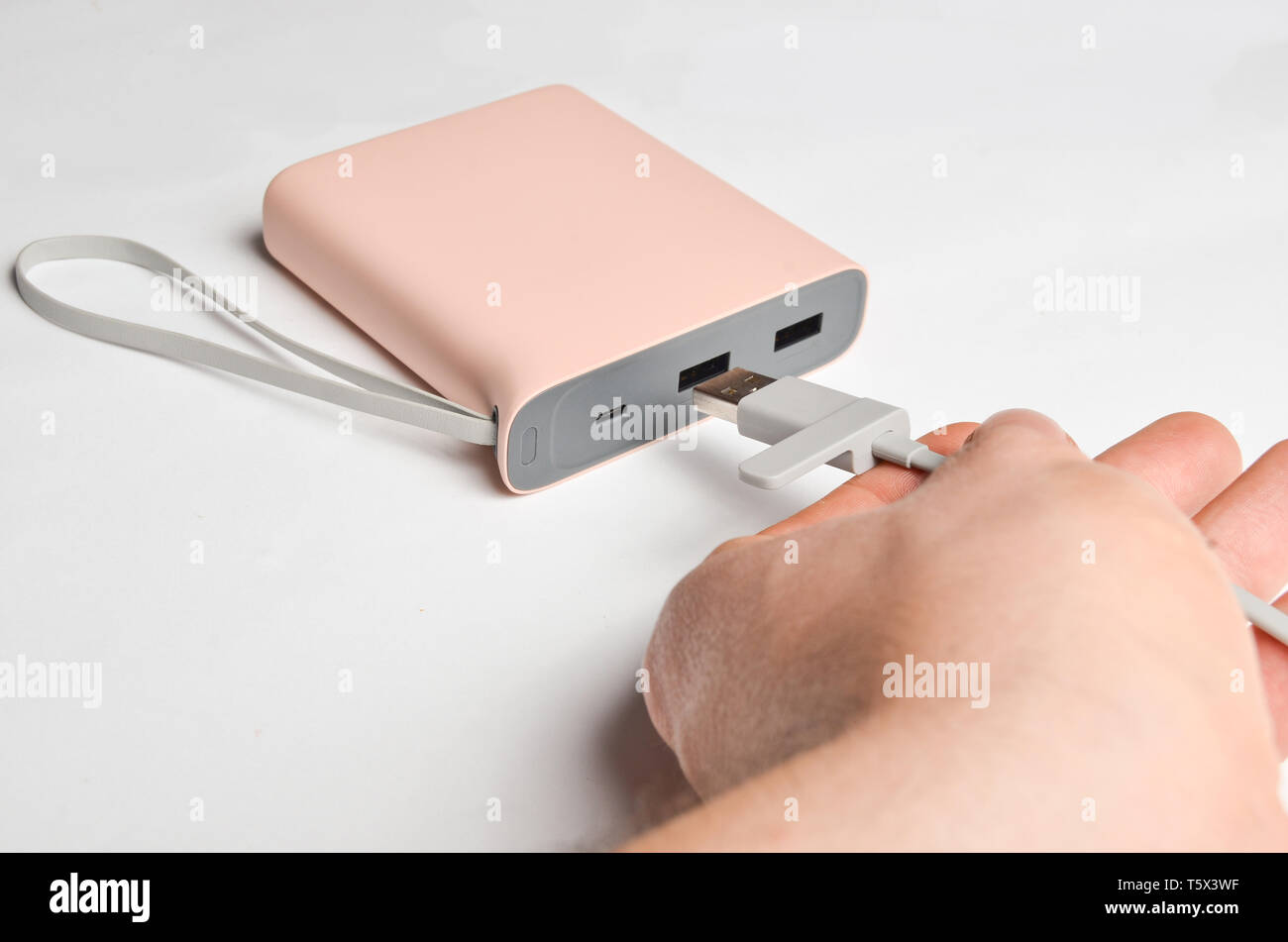 A hand connects a usb cable to a power bank on a white background ...