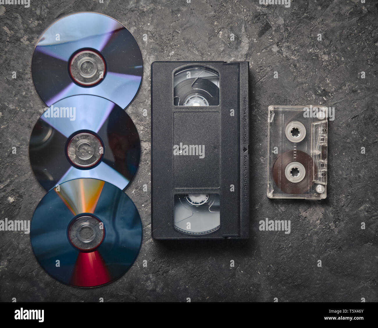 Flat lay video cassettes, CD's, audio cassette on a black concrete ...