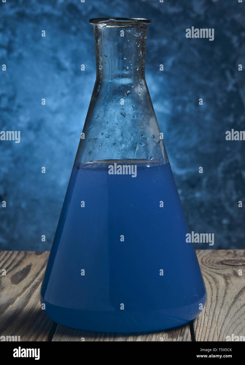 A laboratory flask with a blue liquid on a wooden shelf against a ...