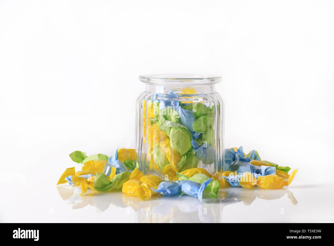 An open glass jar with wrapped candy in and around it Stock Photo - Alamy