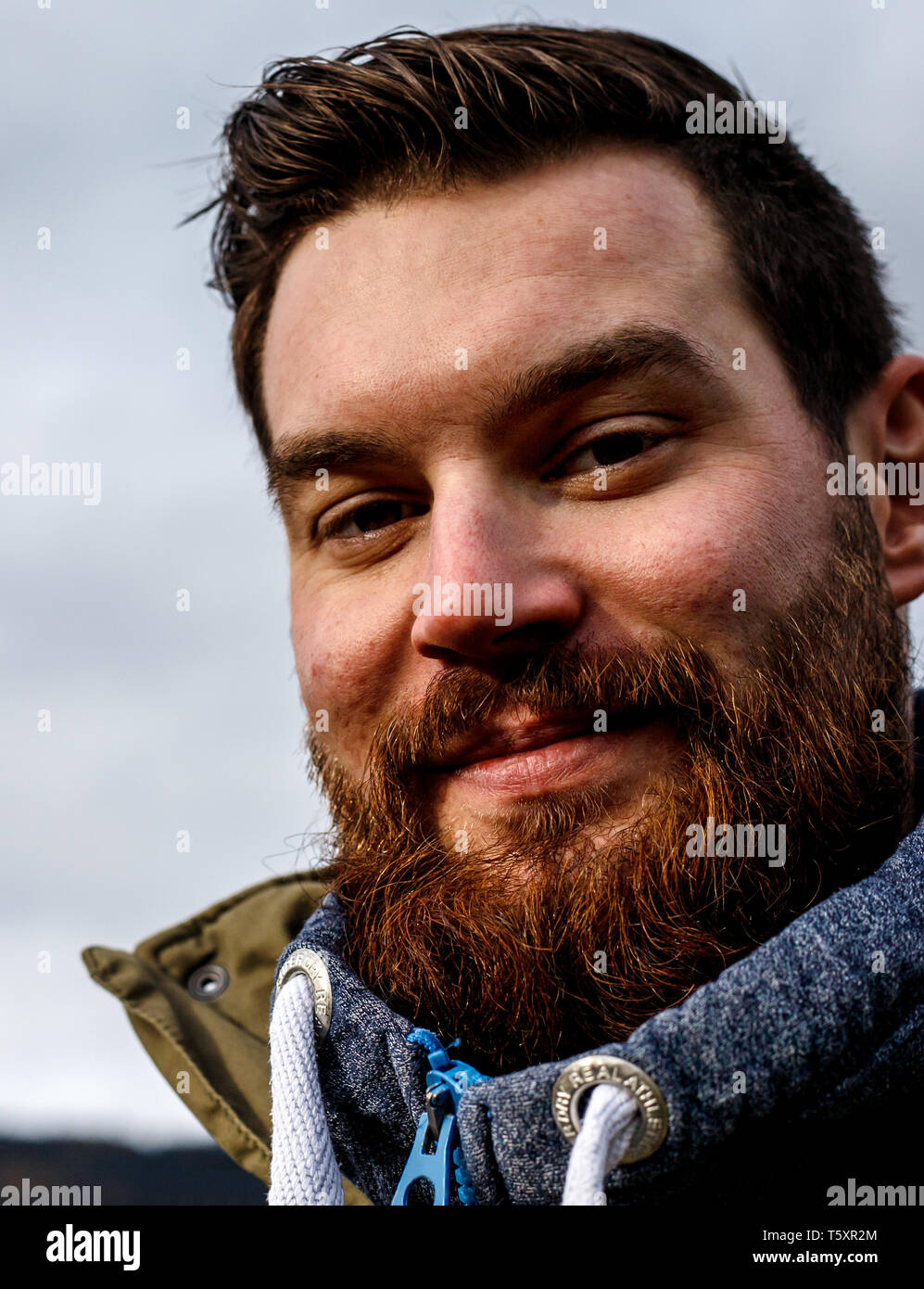 Young attractive bearded man with dark hair and a pullover in the park ...