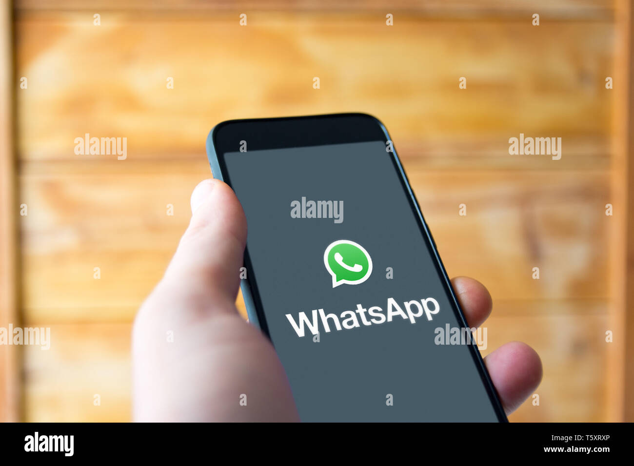 Hand holding smart phone opening popular texting app "Whats App" close ...