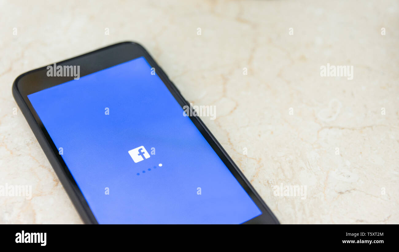 Cell phone with facebook app opening, showing logo and loading screen ...