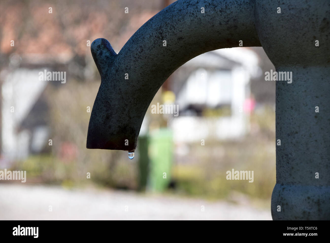 Drop of water from old water well pump with house in the background ...