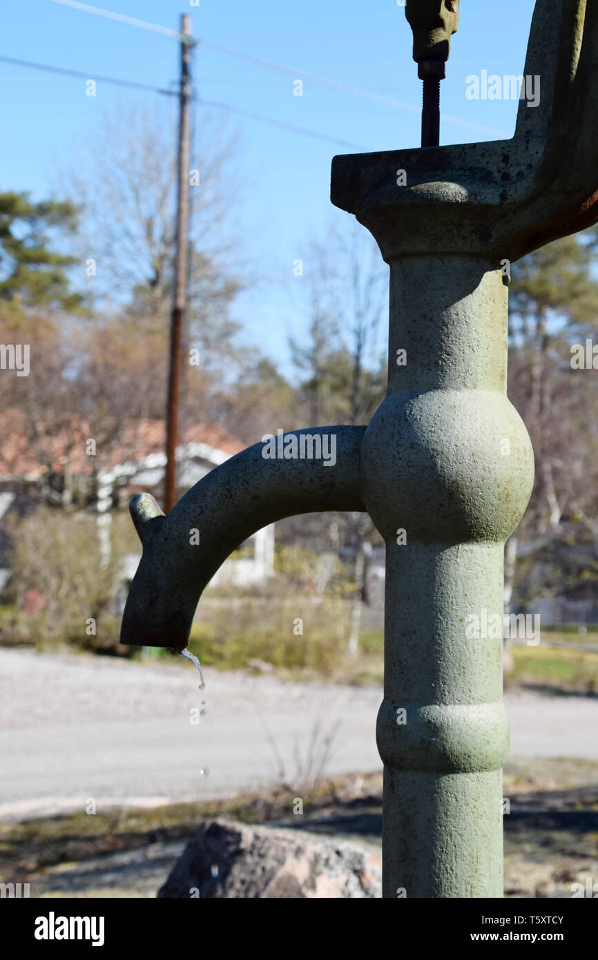 Drops of water from old water well pump with a house in the background ...