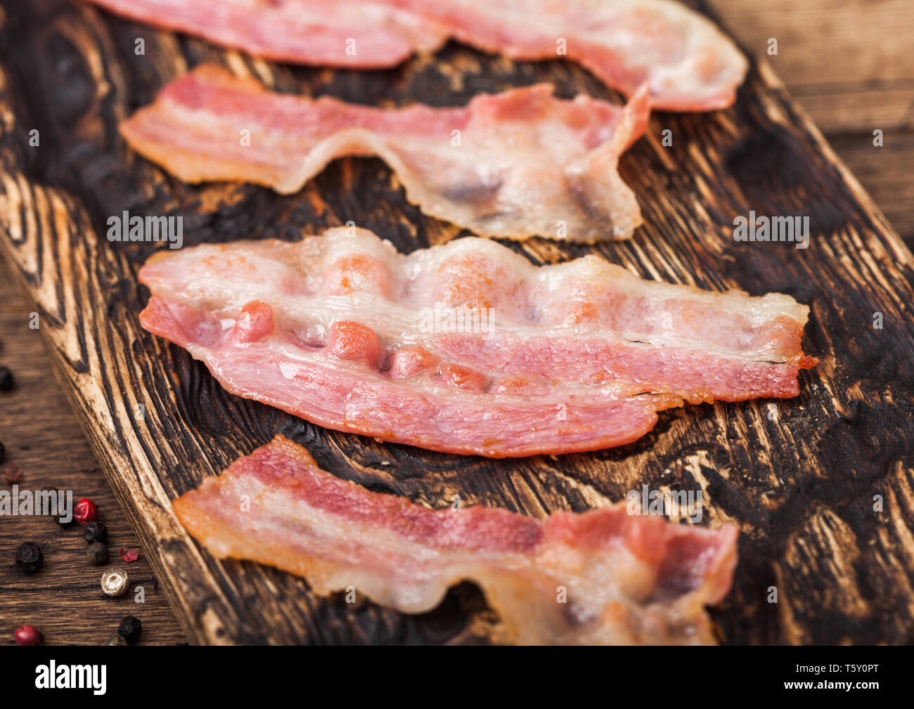 Grilled oily bacon rashers on vintage chopping board close up. Macro ...