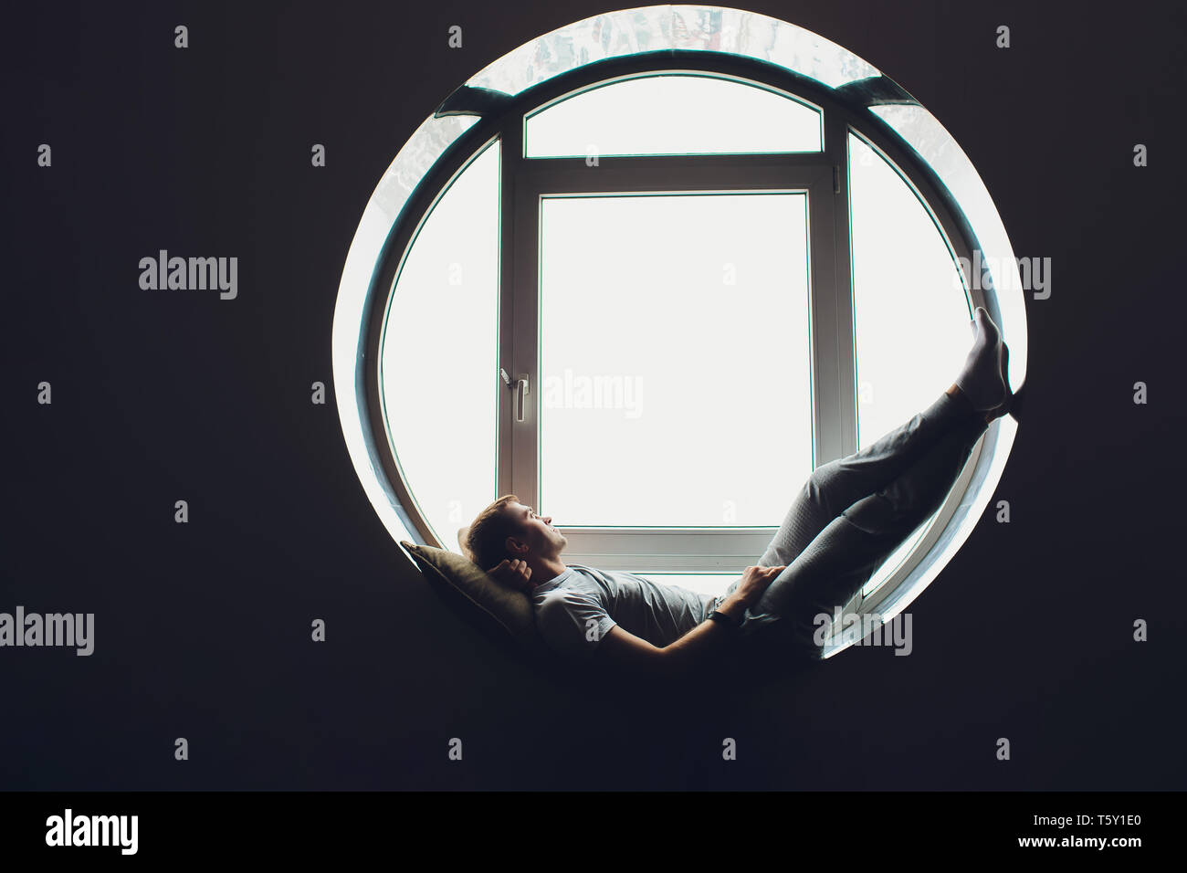 young man sitting in a window looking out over the city . Men enjoy sun ...
