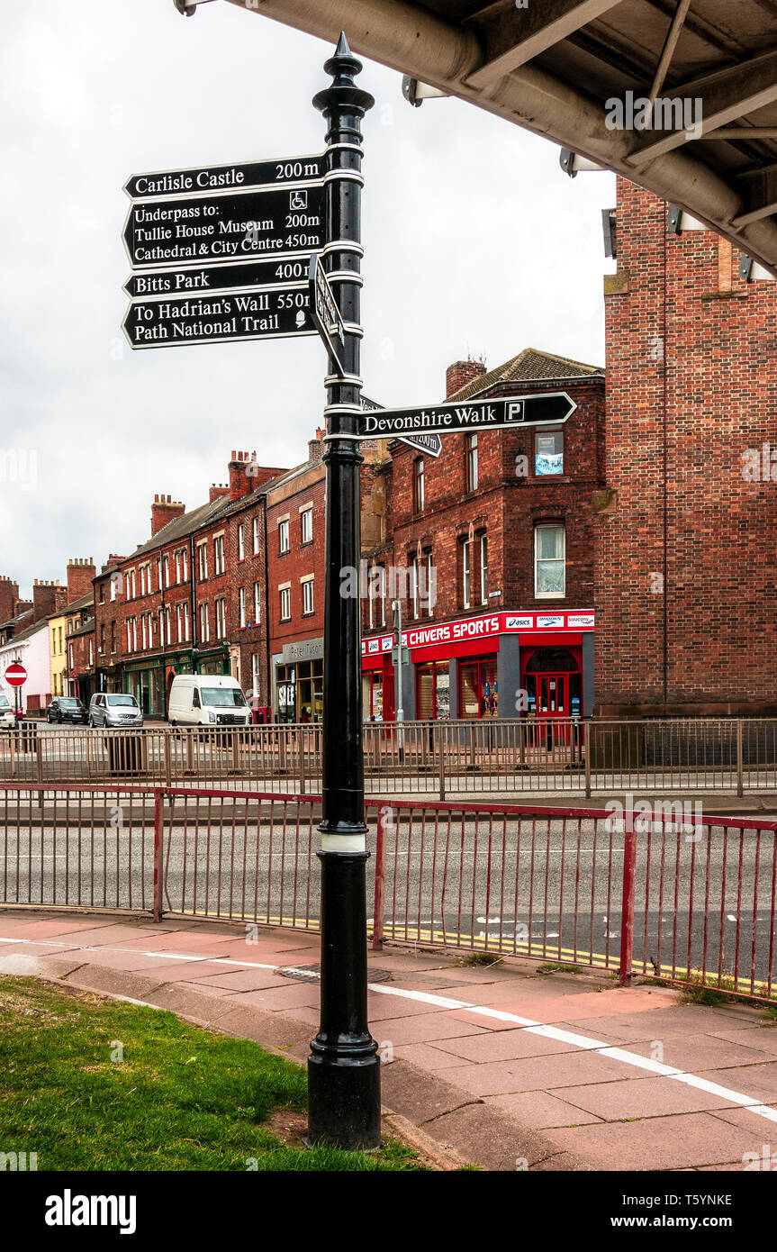A modern signpost standing under the overhead footbridge spanning a ...