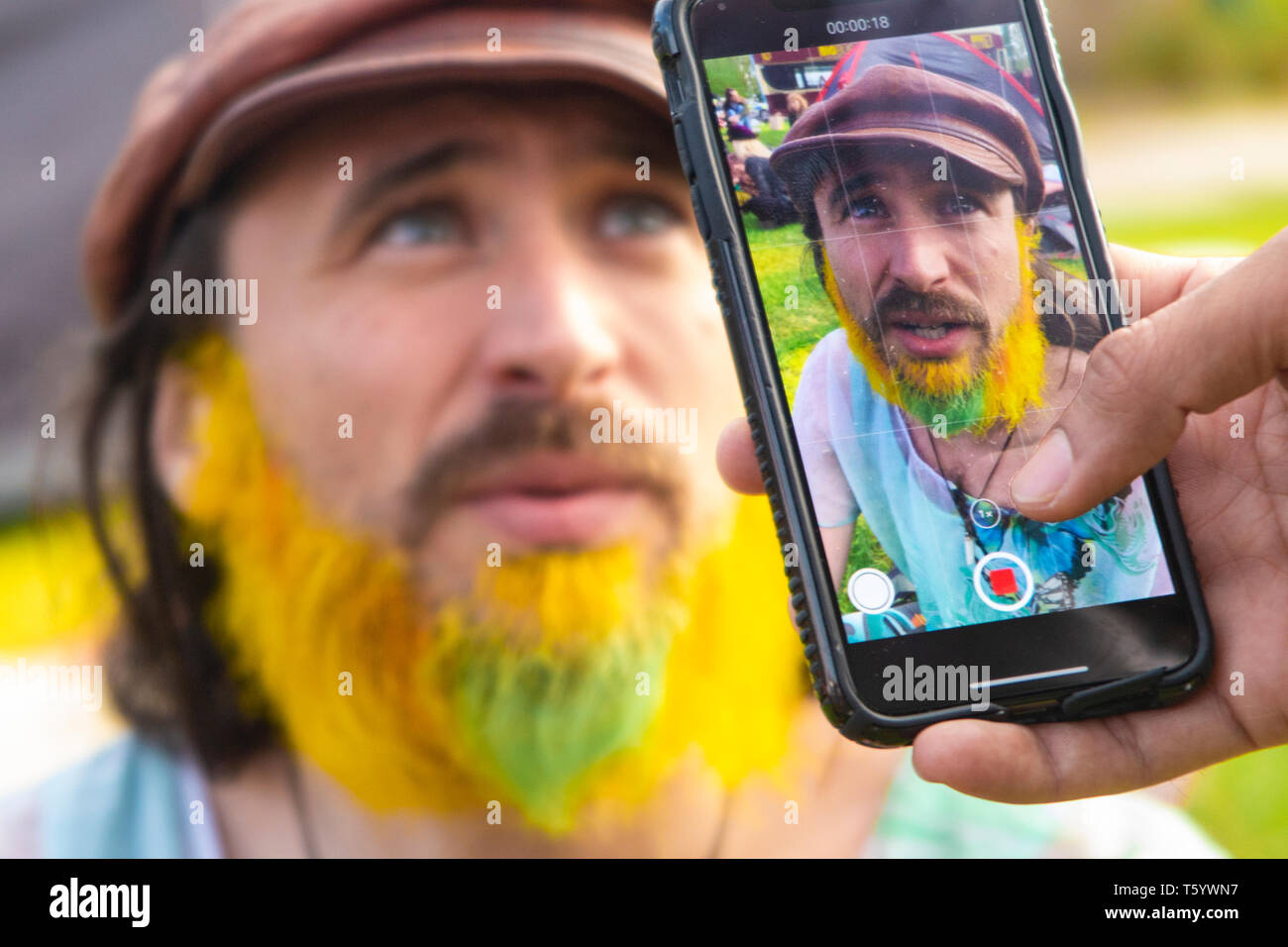 A man with a yellow and green beard is interviewed at the Closing ...