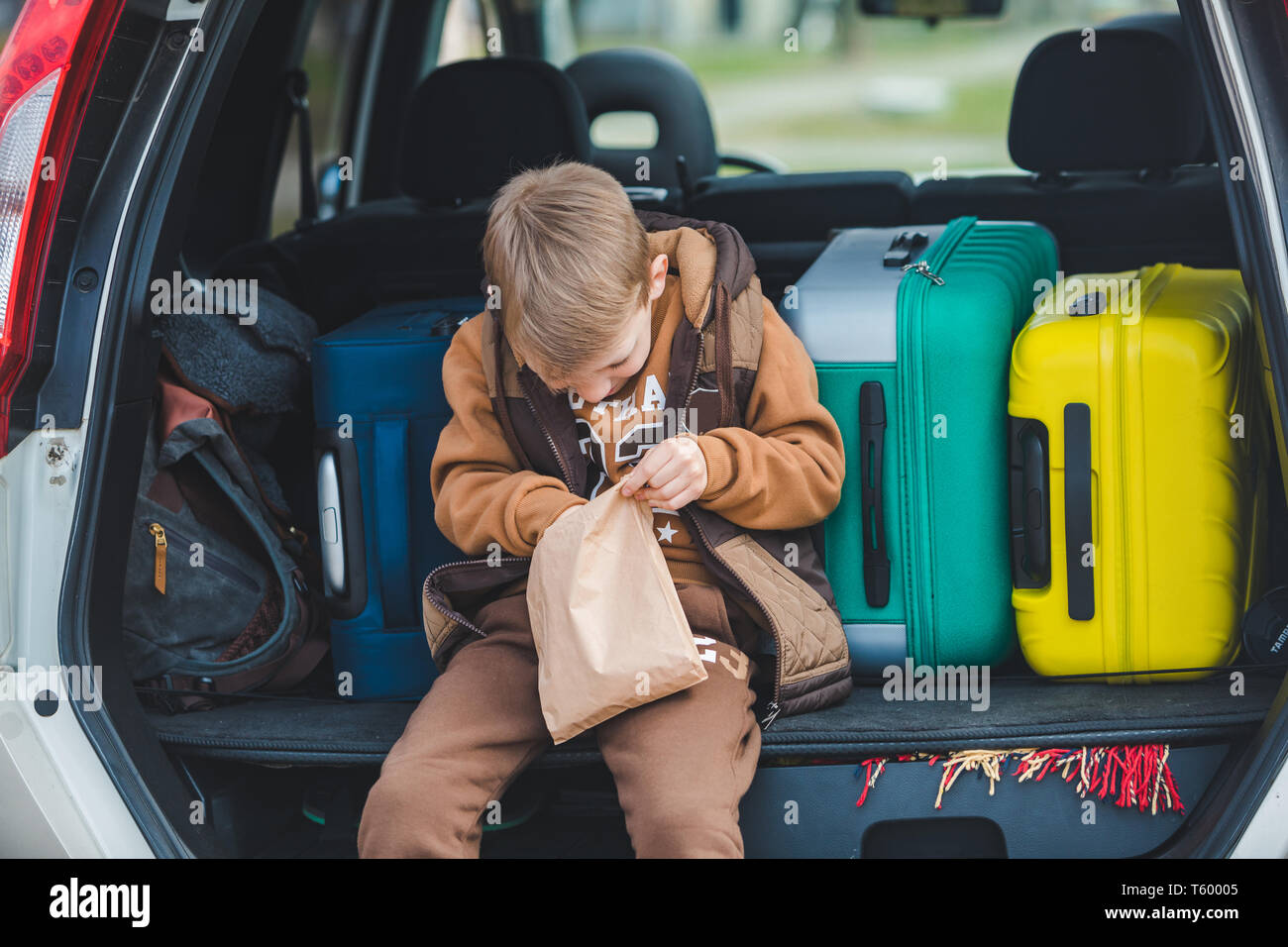 little kid looking into paper bag with candies sitting in car trunk ...